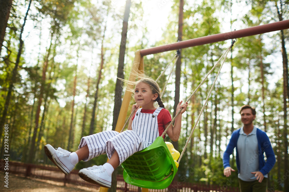 Cute little girl enjoying chill with her dad while sitting on swing in ...