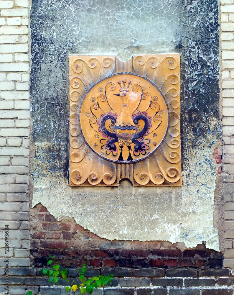 Damaged cement low relief of a peacock bird on a brick wall with paint ...