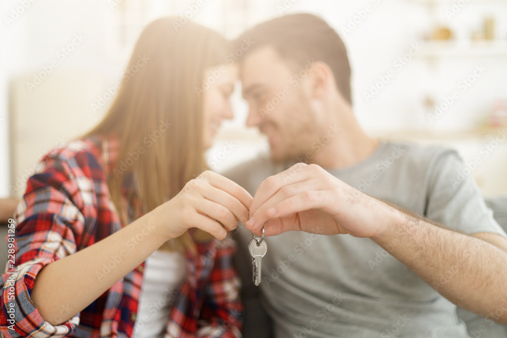 Young happy smiling couple holding set of keys, sitting on sofa face to ...