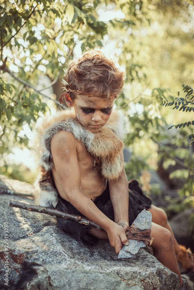 Caveman, manly boy making stone axe. Funny young primitive boy outdoors ...