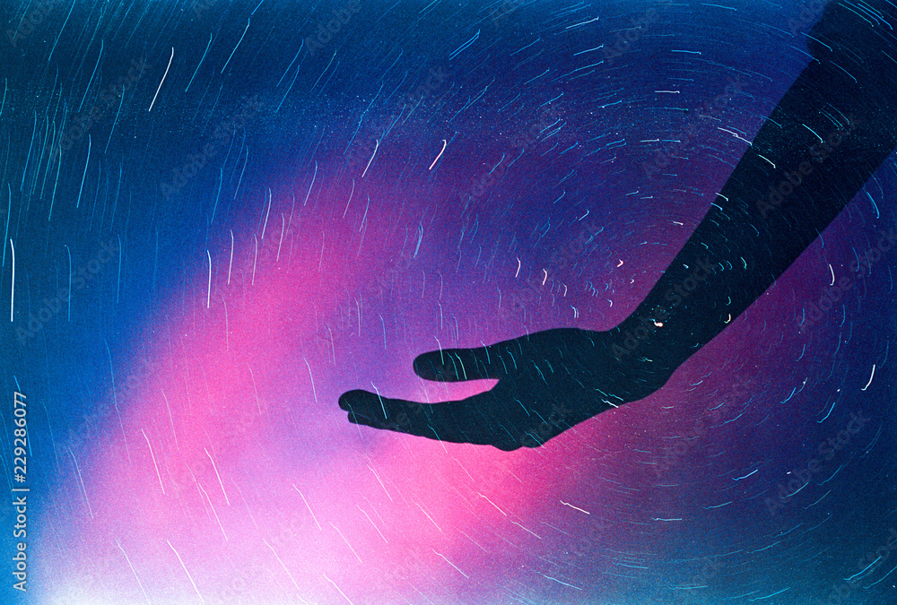 Silhouette of an outstretched hand surrounded by swirling star trails ...
