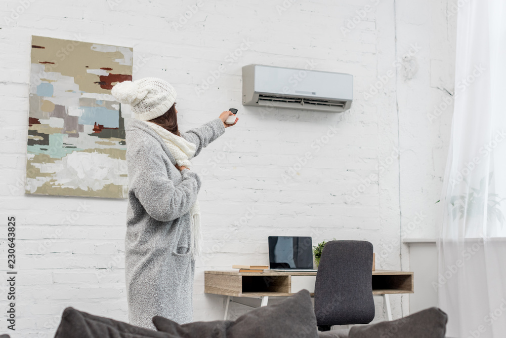 beautiful young woman in warm clothes pointing at air conditioner with ...