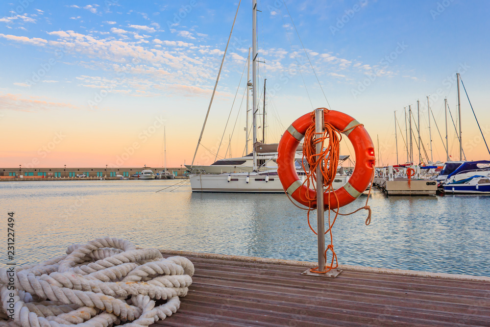 the quay of a marina at the sunset /a mooring rope with a lifebelt on ...