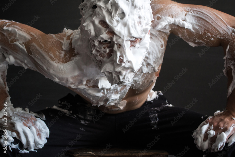 portrait of a muscular guy smeared with shaving foam sitting and ...