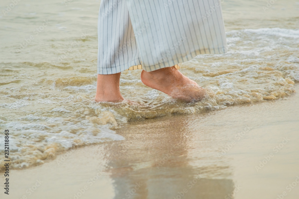 The foot of a woman wearing white pants standing on the baech have sae ...