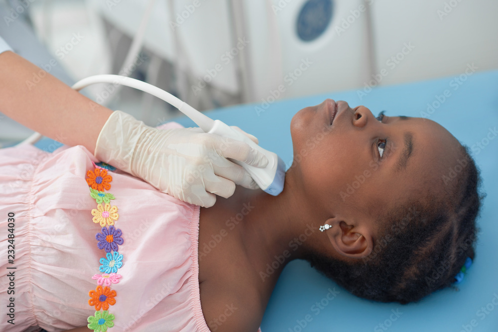 Little afro girl lying on bed while ultrasound of thyroid. Stock Photo ...