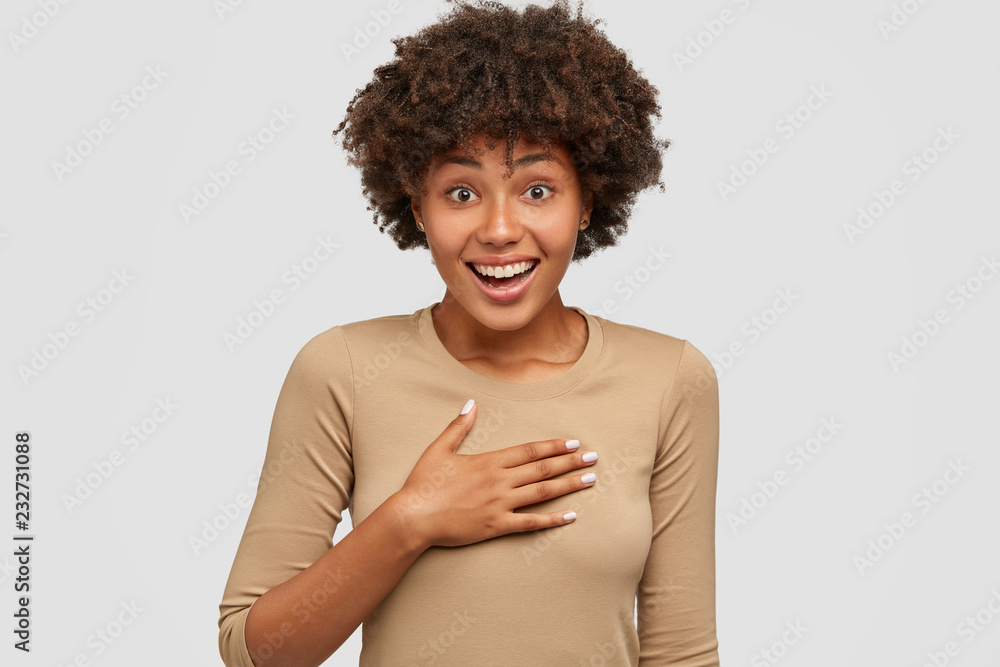 Thrilled glad dark skinned woman keeps hand on chest, surprised to ...