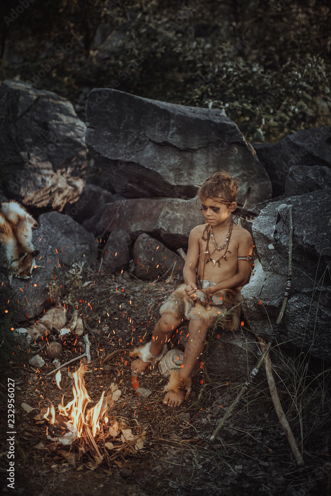 Caveman, manly boy at the fire. Scary young primitive boy outdoors near ...