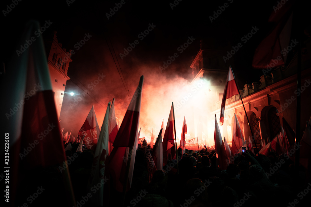 Foto People carry Polish flags and burn flares as they walk across the ...