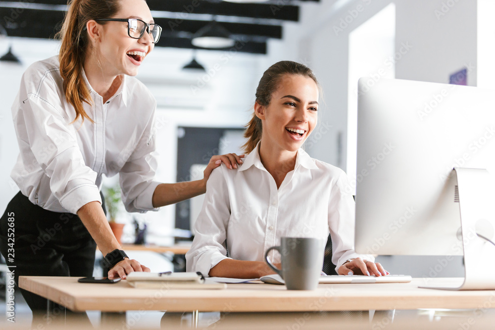 Happy cheerful colleagues business women in office working while using ...