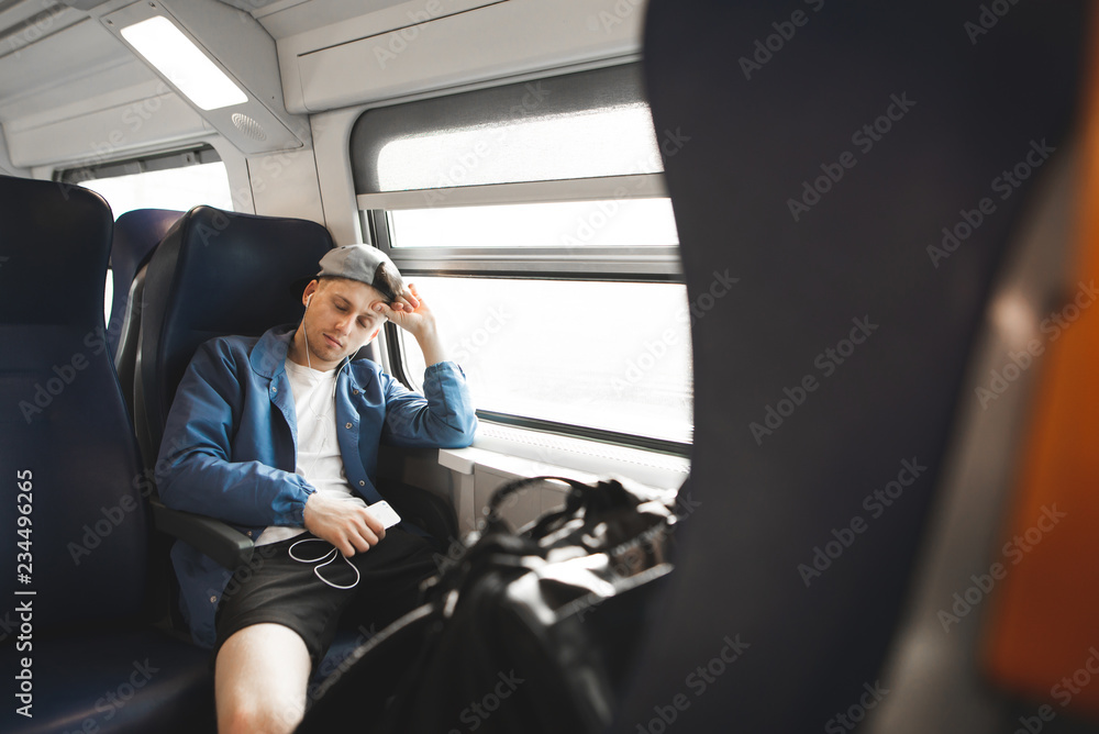 Young man sleeping in a train near the window with headphones and a ...