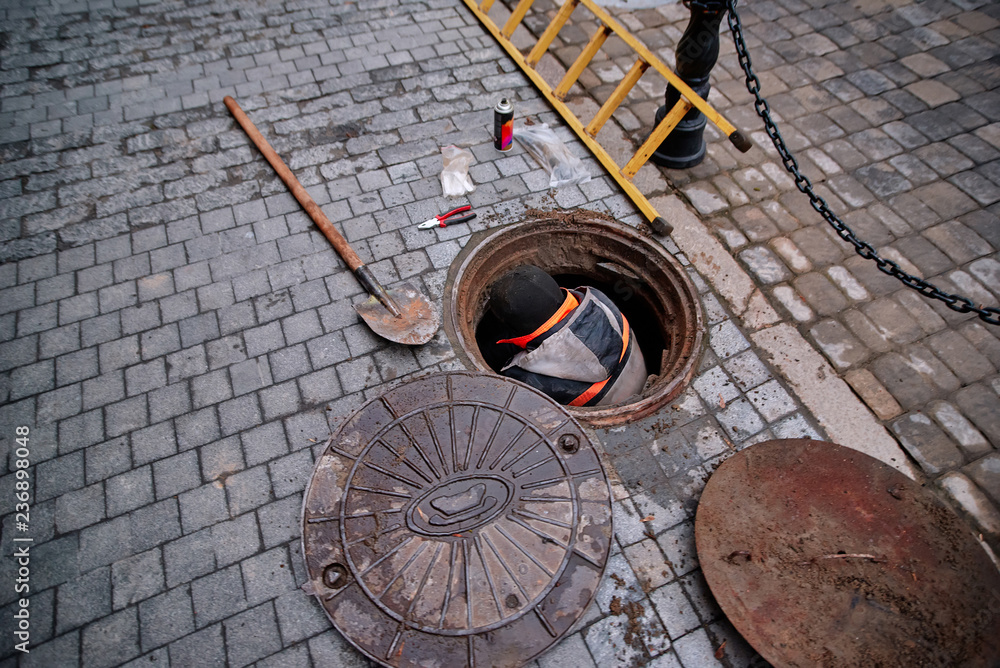 Working man comes out from the sewerage hatch in the ground on city ...