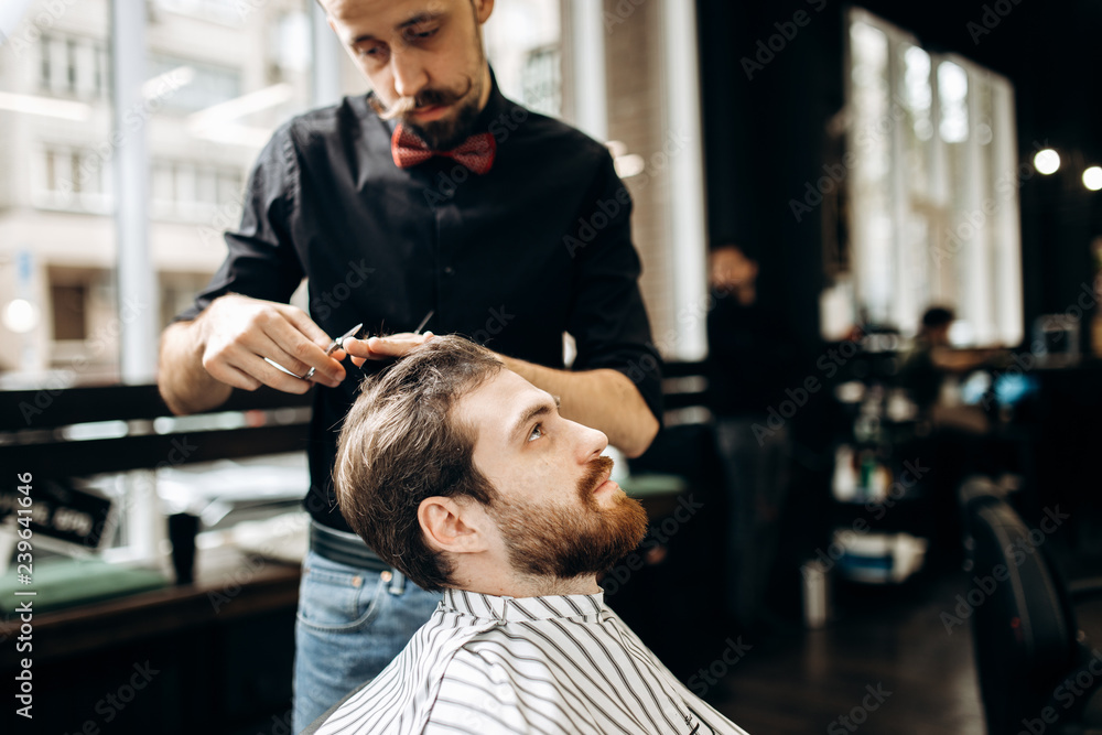 Mustachioed barber dressed in a black shirt with a red bow tie makes a ...