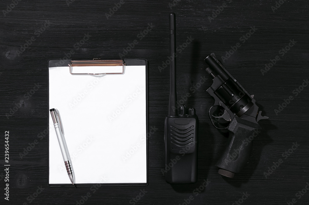 Blank paper page, pen, portable radio station and handgun on a black ...