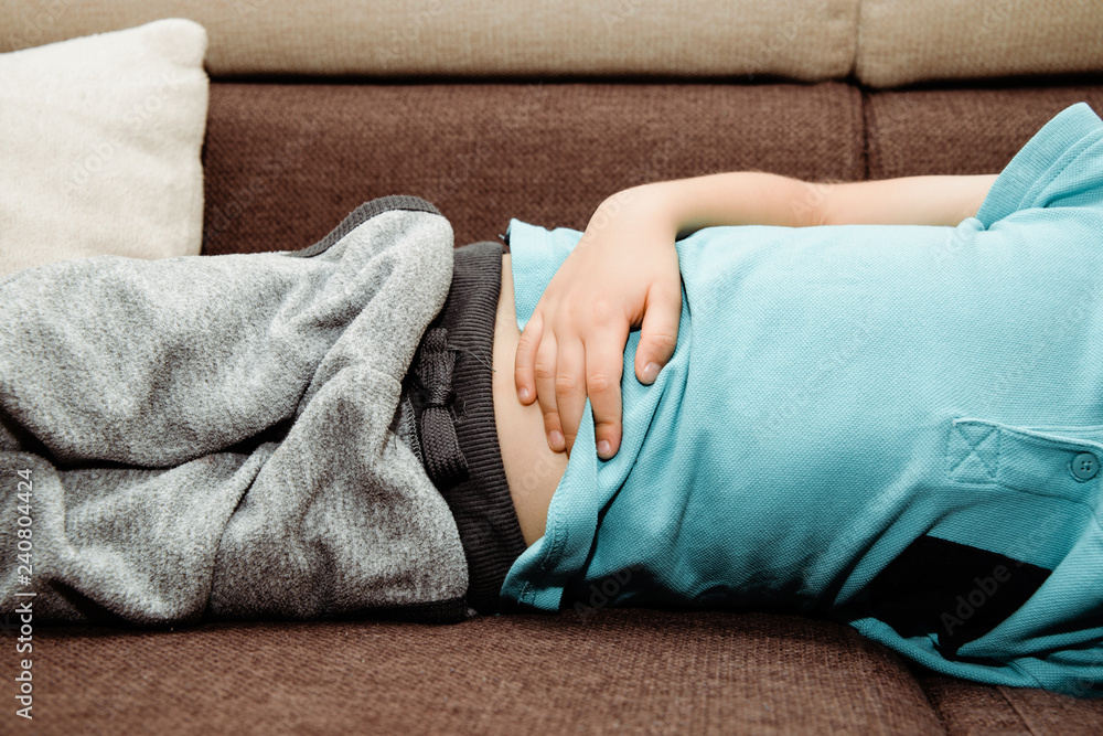 A little boy, the child is lying on the bed and holding his belly. Baby ...