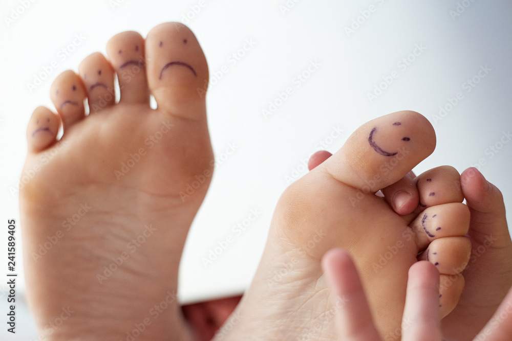 Female toes with painted smileys and children's hands. Foot care ...