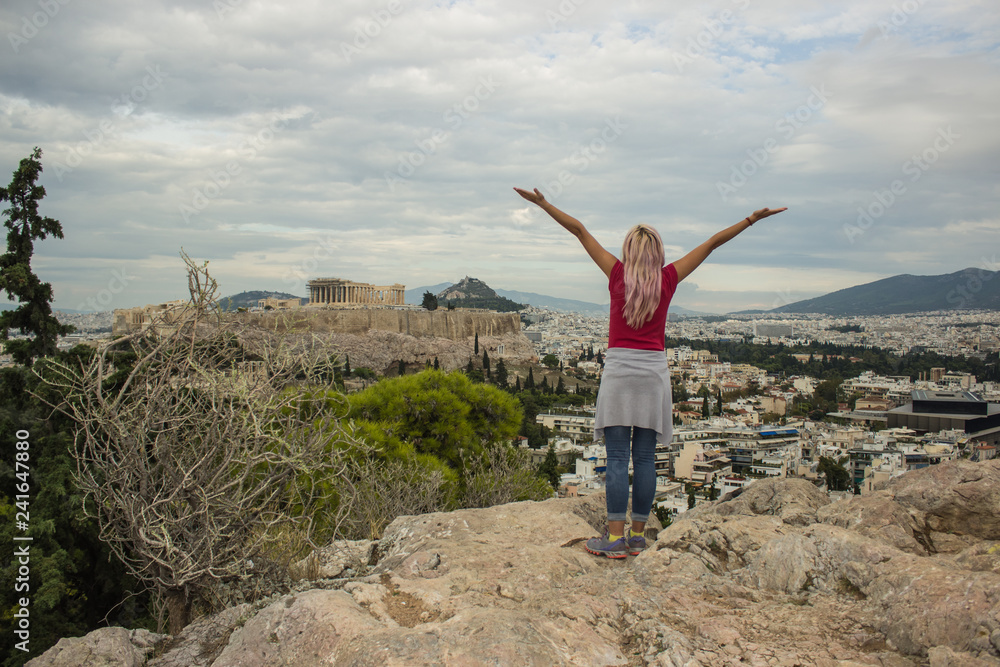 travel girl back to camera in freedom pose with hand up on top of rock ...