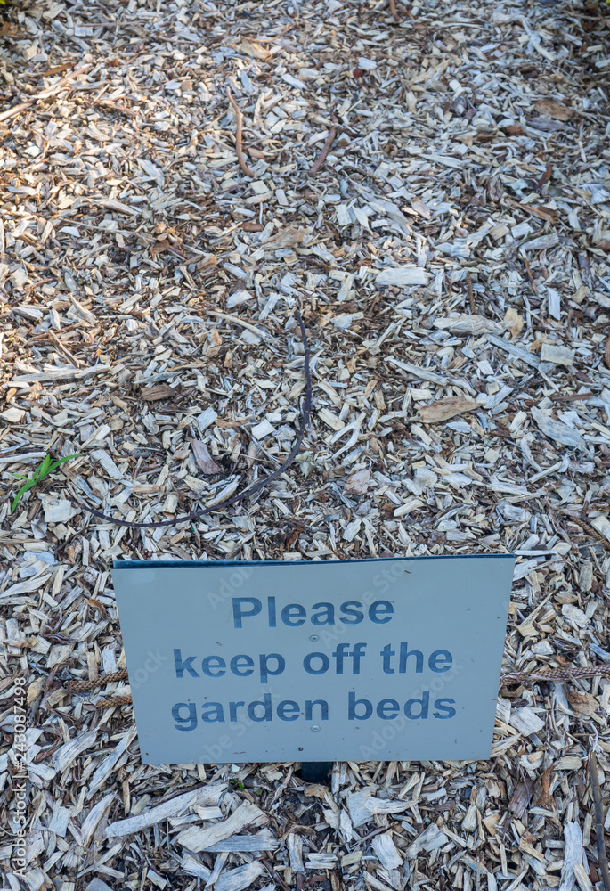 "Please keep off the garden beds" a square warning sign on empty flower ...
