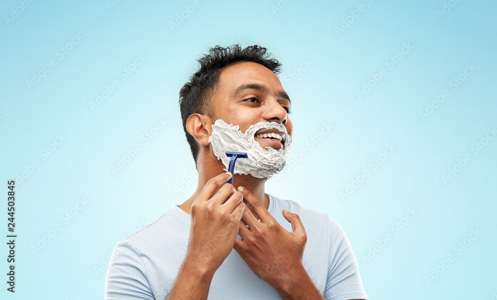 grooming and people concept - young indian man shaving beard with ...