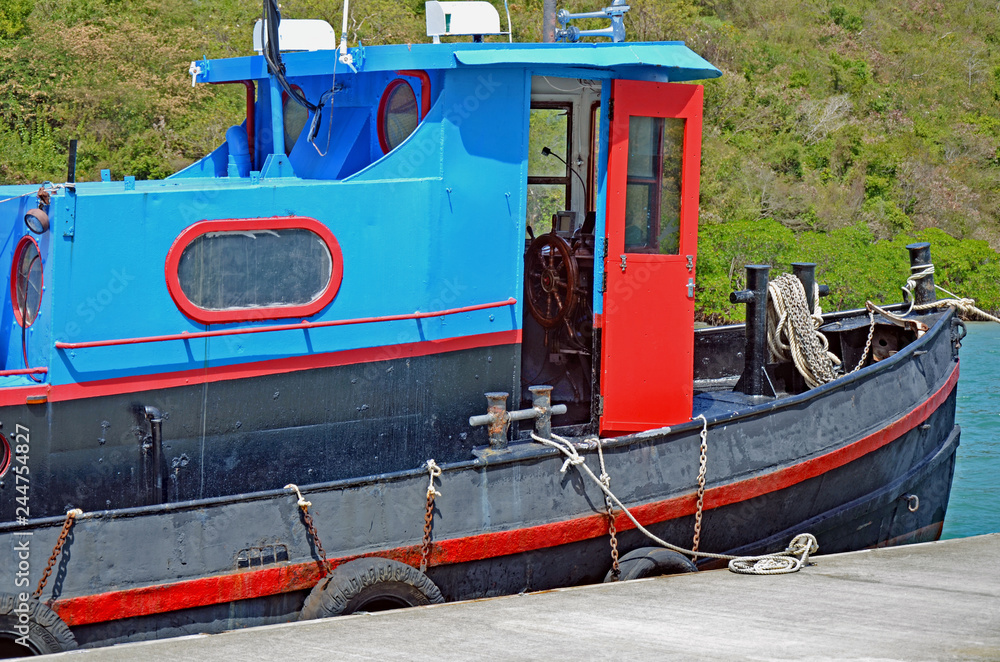 The side of a brightly painted red, blue, and black tug boat tied to a ...