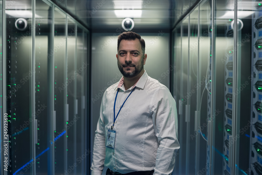 Adult IT worker in white shirt standing among server racks in data ...