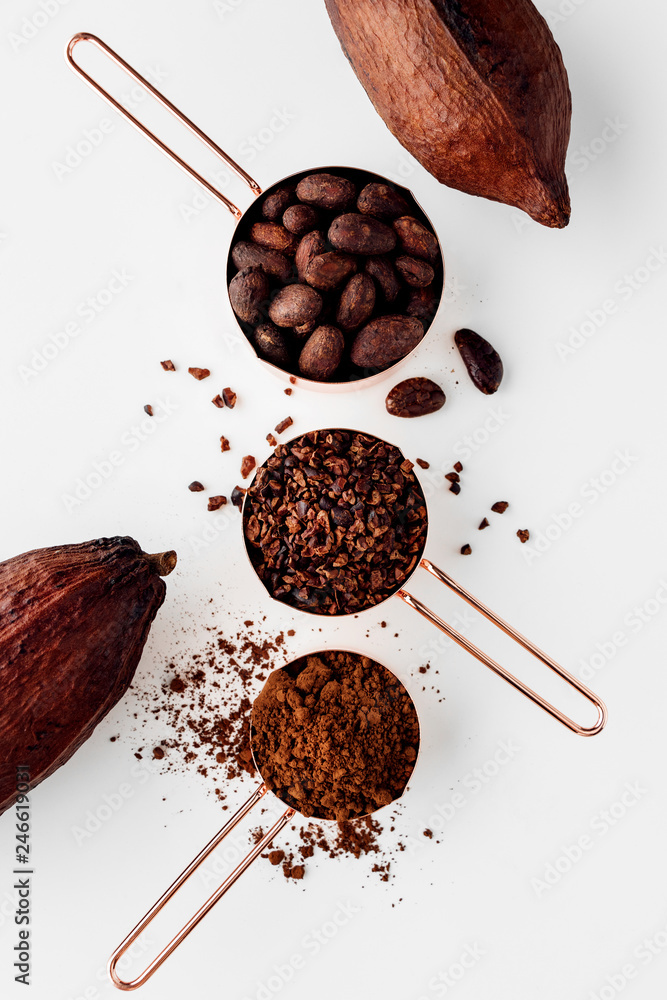 Rose gold measuring cups of cocoa beans, cacao nips, cocoa powder and ...