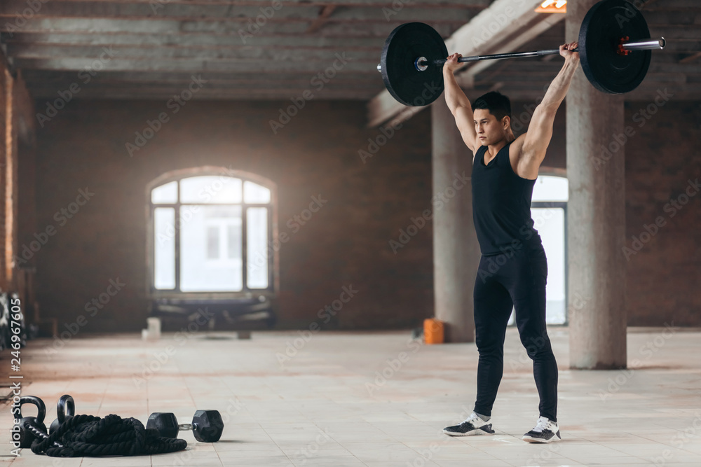 strong man holding heavy weights over his head at gym. full length side ...