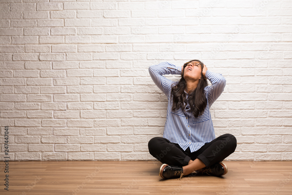Young indian woman sit against a brick wall frustrated and desperate ...