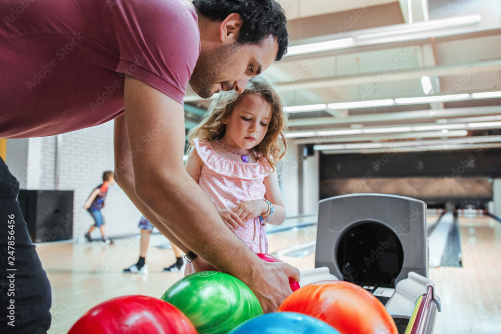 Father and daughter having fun at bowling alley. Choosing a ball color ...