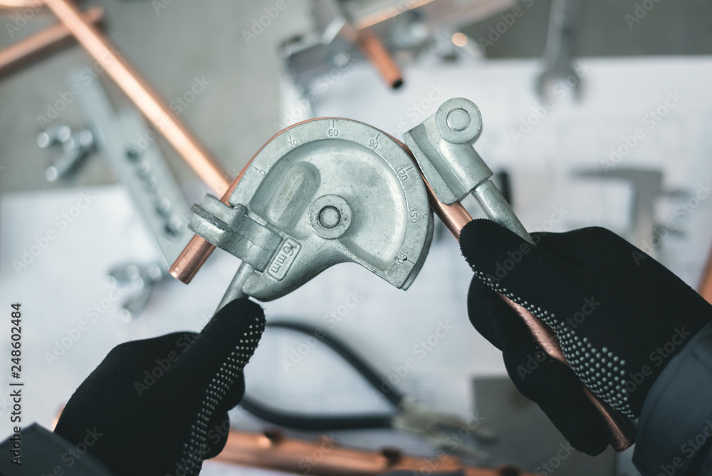 Pipe bender tool in a hands of factory worker on a factory workbench ...
