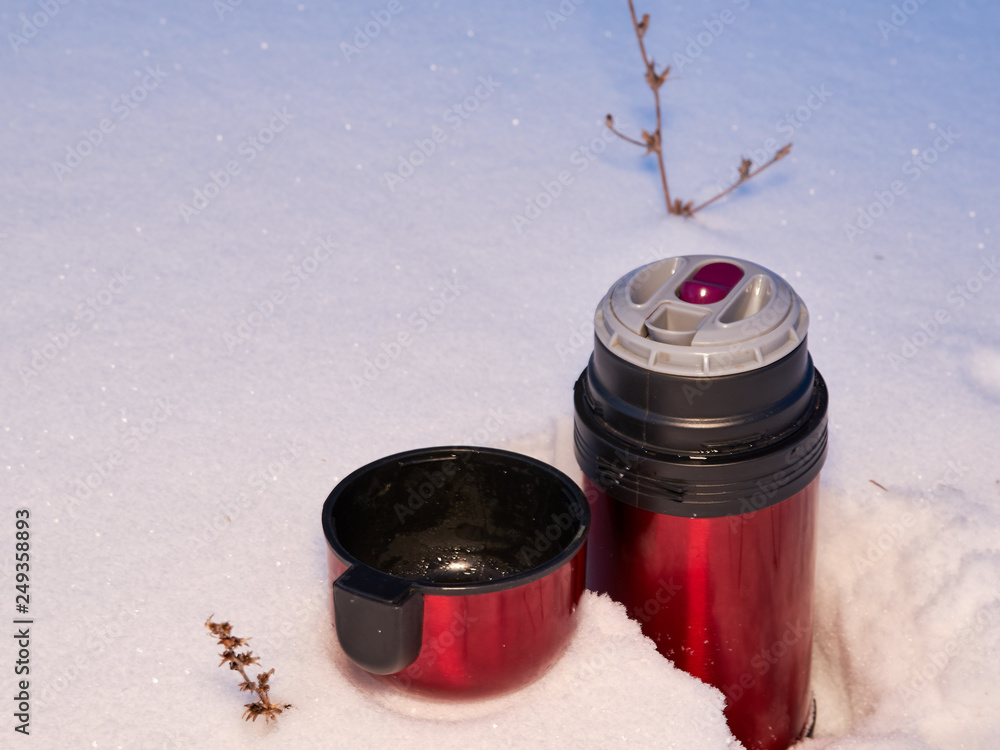 big red tea thermos with the lid open on the snow in the woods in the ...
