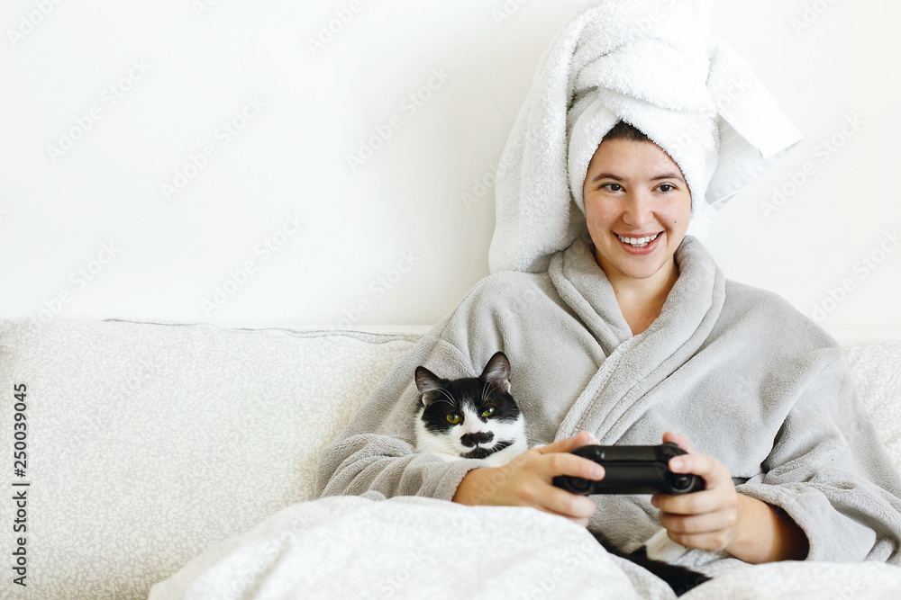 Happy girl playing video games with cat in bed. Beautiful young woman ...
