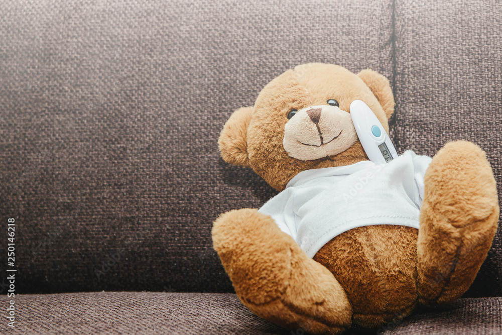 A small plush teddy bear measures a fever with an electronic ...