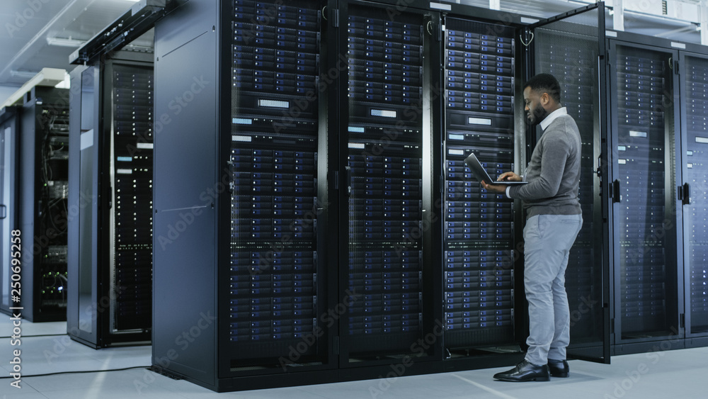 Black IT Specialist is Working on Laptop in Data Center while Standing ...