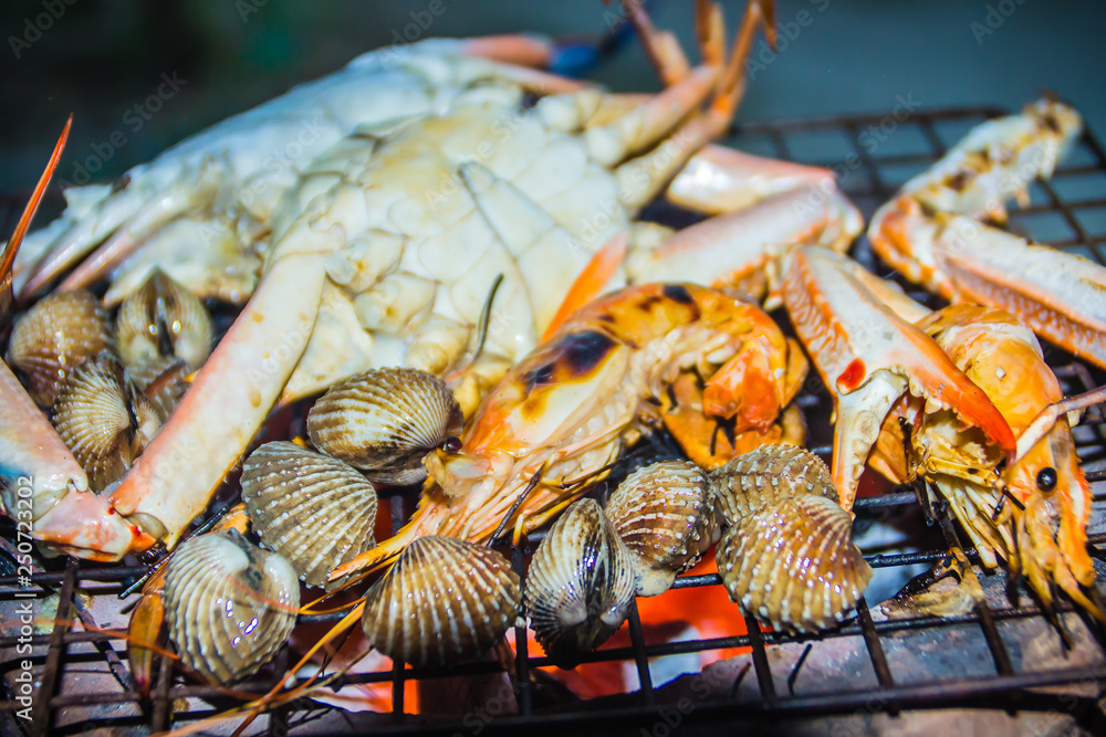 Close up grilled crabs and clams on fire charcoal stove at night party ...