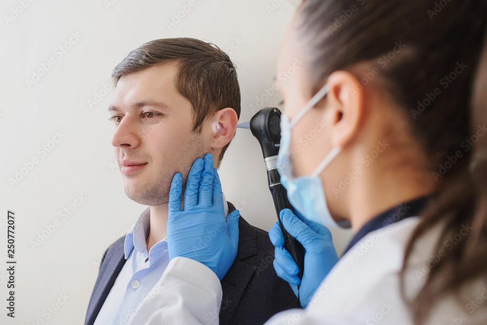 close up photo of a female otolaryngologist examining the ear of a male ...