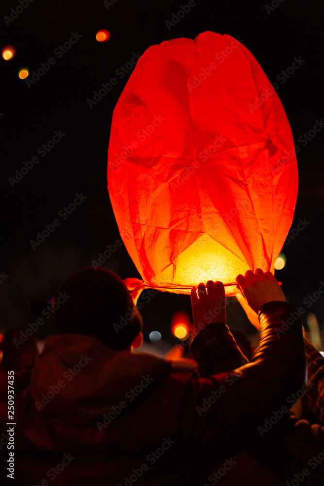 Two people work together to hold a floating lantern while it warms up ...