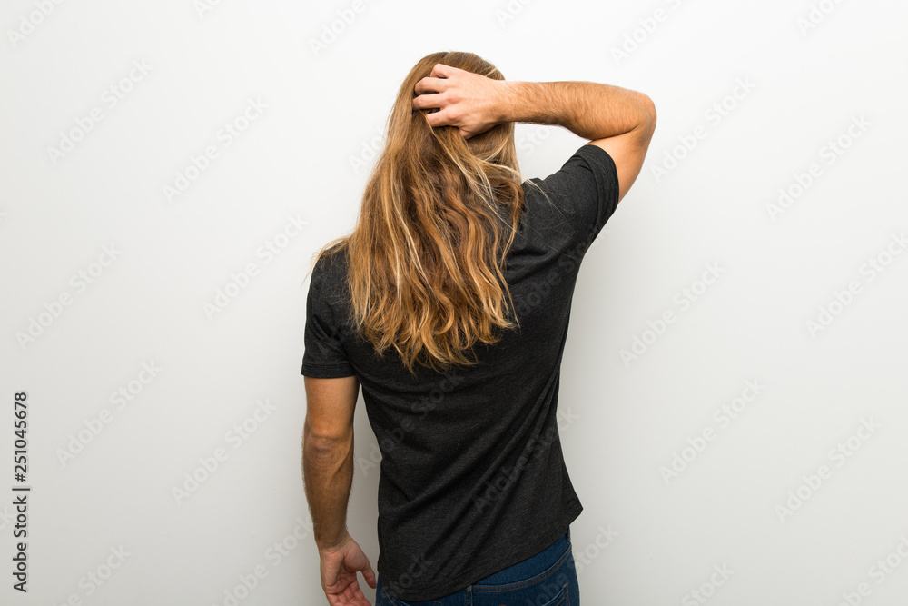 Blond man with long hair over white wall on back position looking back ...