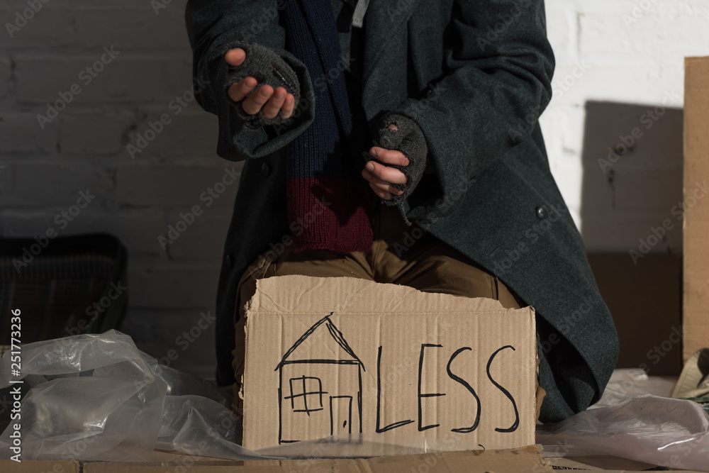 partial view of begging man with symbol of house and "less" inscription ...