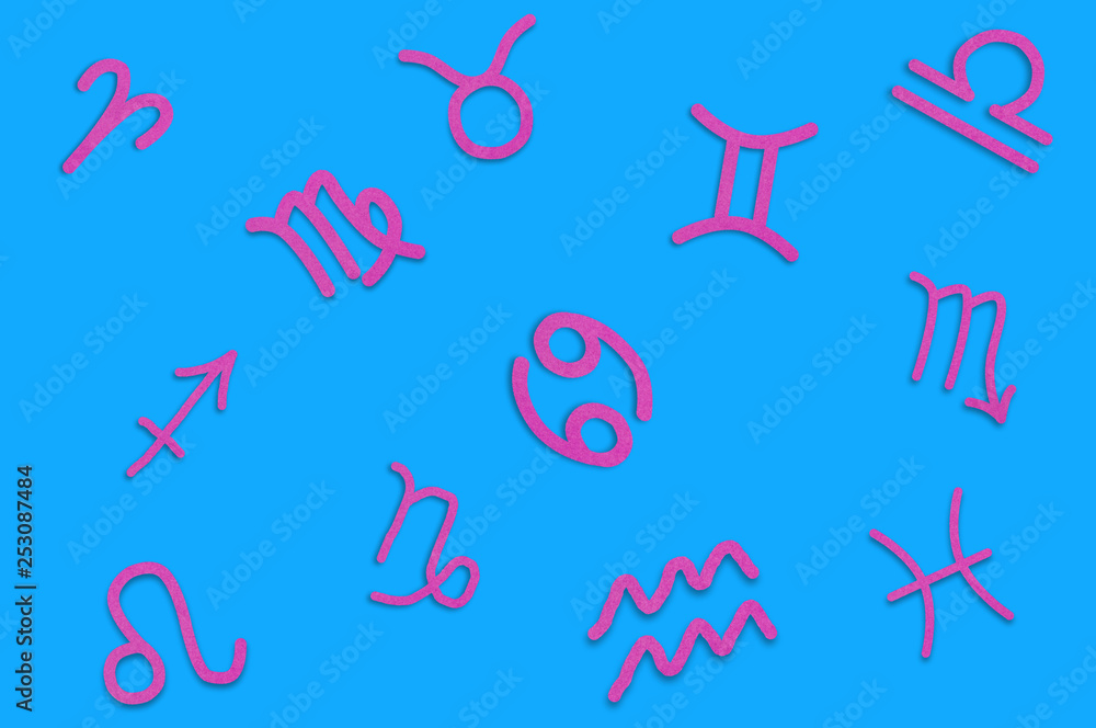 Set of zodiac signs cut out of purple paper scattered on blue table ...