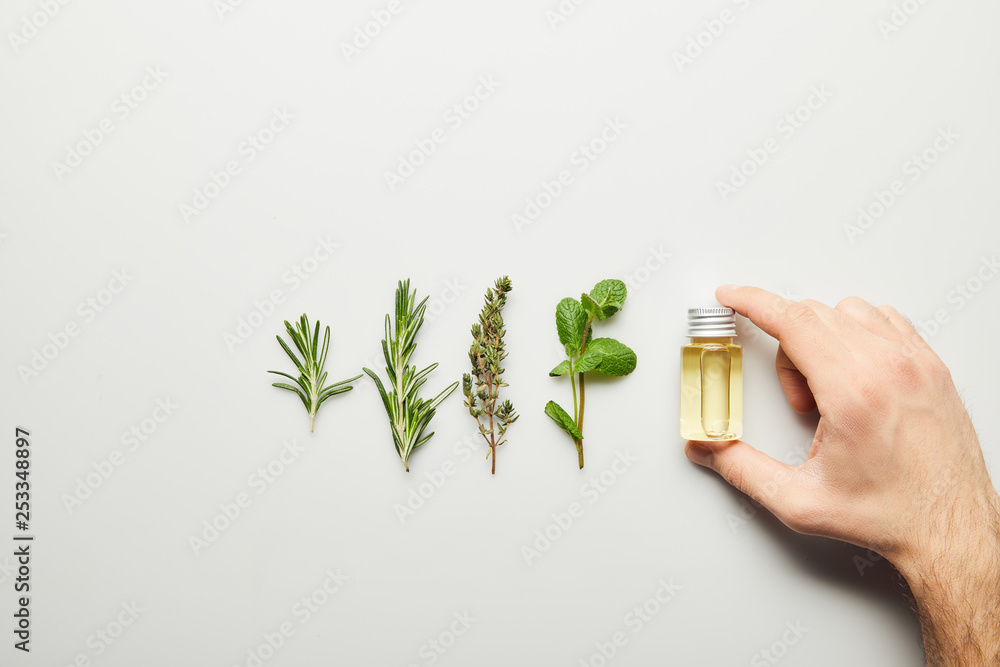 Partial view of man holding bottle of essential oil on white background ...