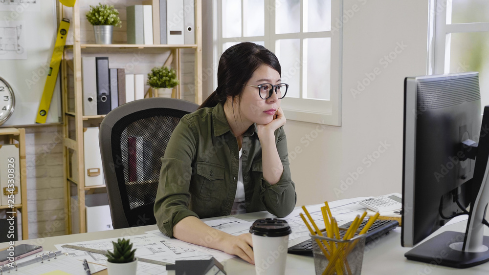 Bored woman architect in glasses looking at desktop monitor in office ...