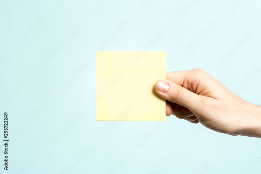Only one hand showing a yellow empty adhesive note on blue background ...