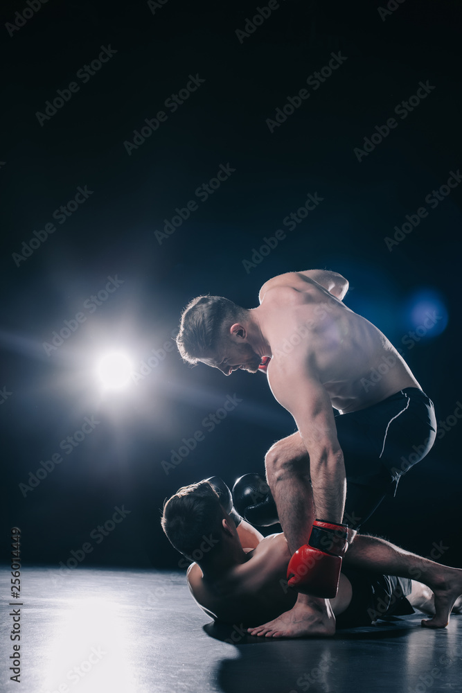 shirtless strong mma fighter in boxing gloves standing above opponent ...