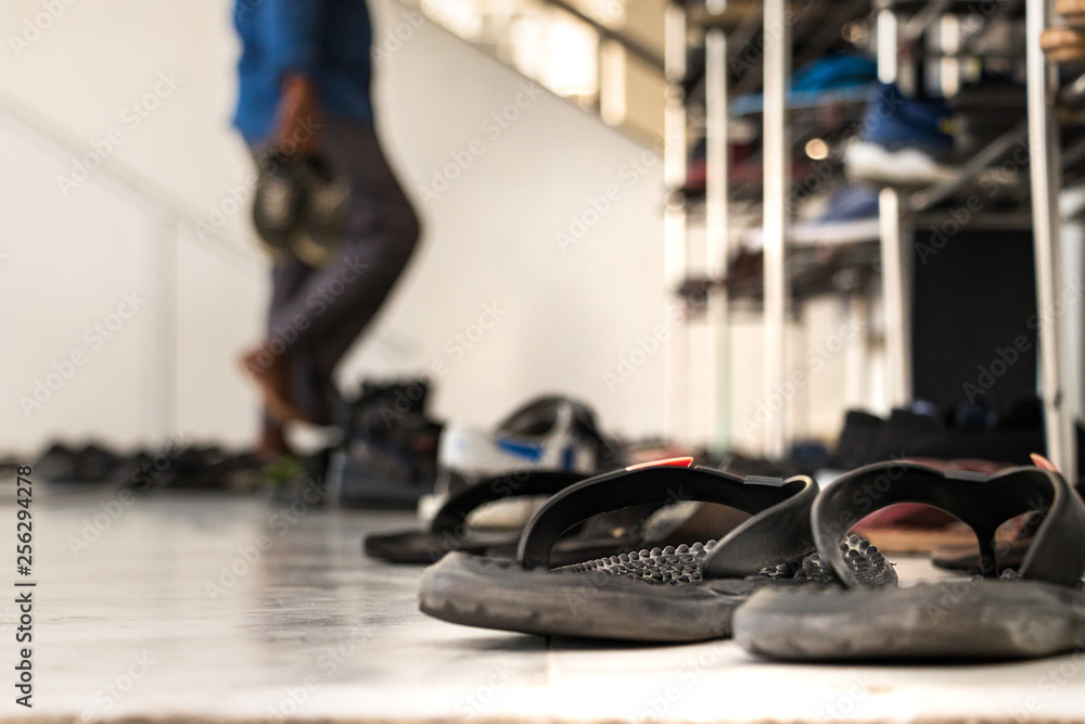 Sandals outside the main entrance of a mosque with a prayer taking off his shoes as blur ...