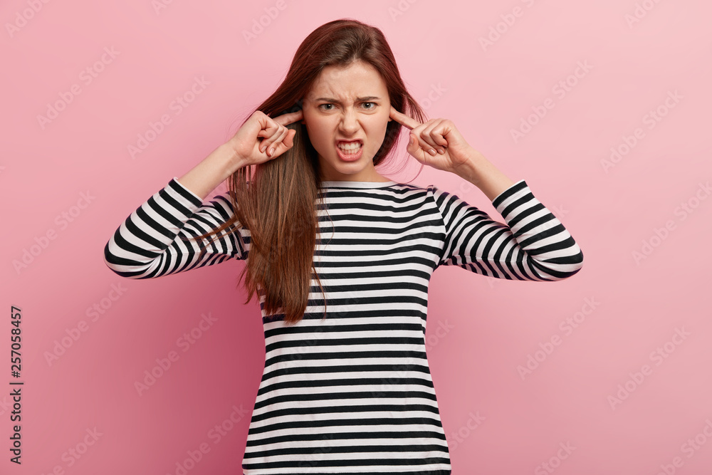Photo Stock Waist up shot of beautiful dissatisfied woman plugs ears as ...