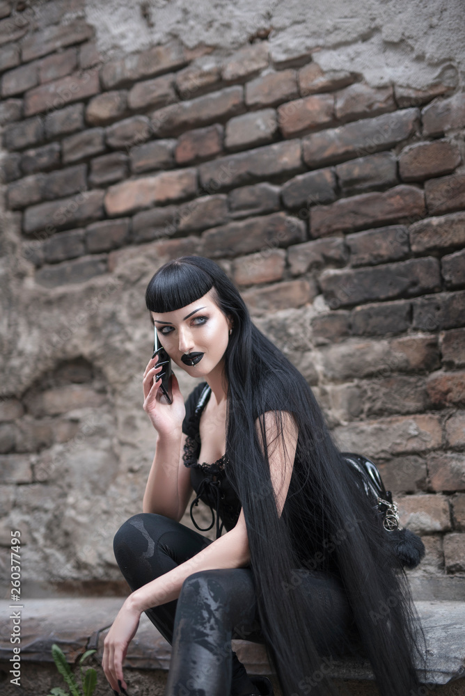 Urban goth girl talking over her cell phone, sitting in an urban ...
