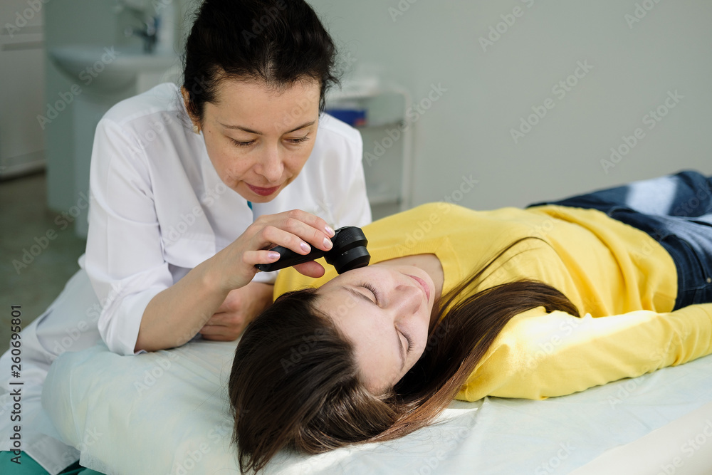 Female dermatologist using a professional dermatoscope while doing skin ...