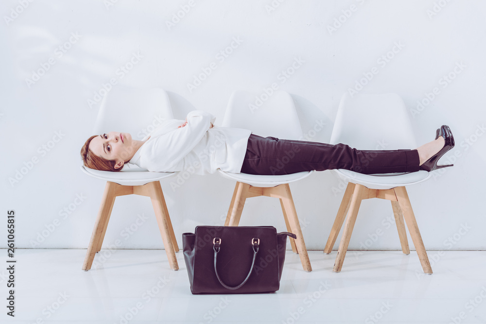 attractive employee lying on chairs near bag while waiting job ...