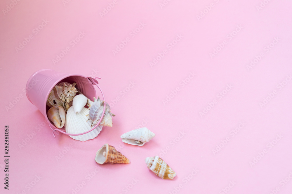 Sea shells of various sizes are scattered from a pink bucket on a pink ...